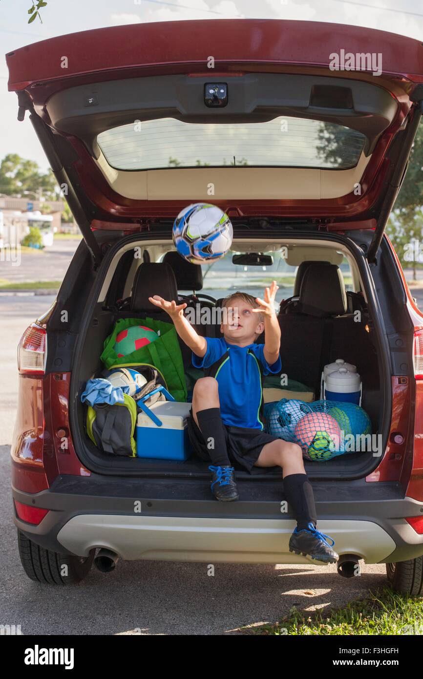 Boy football player sitting in car boot throwing and catching football ...