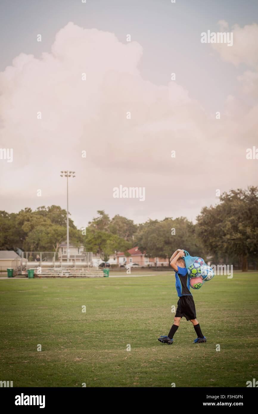 Boy football player carrying bag of footballs on practice pitch Stock ...