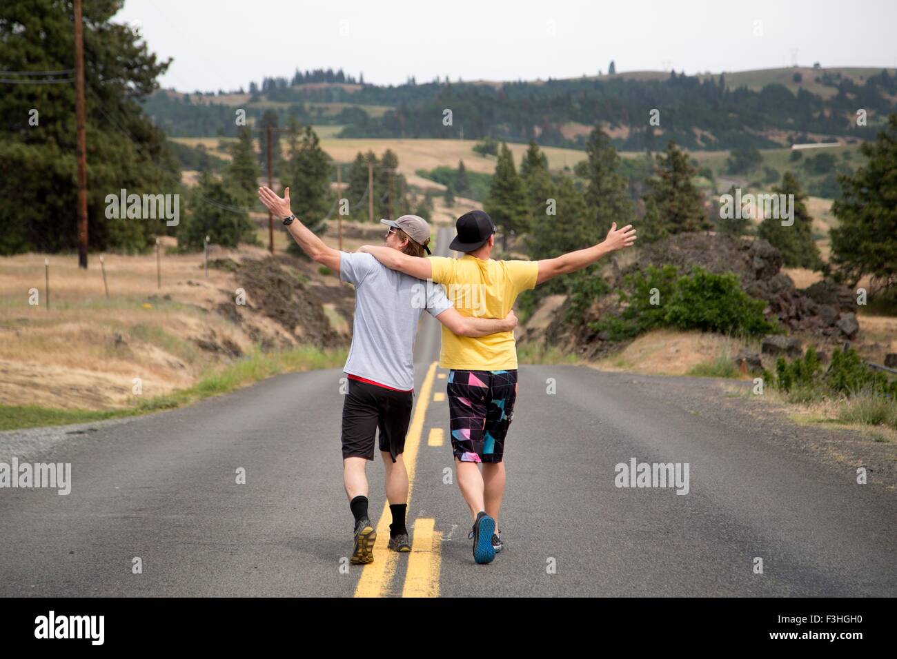 Two men walking along road together, arms raised, appreciating view ...