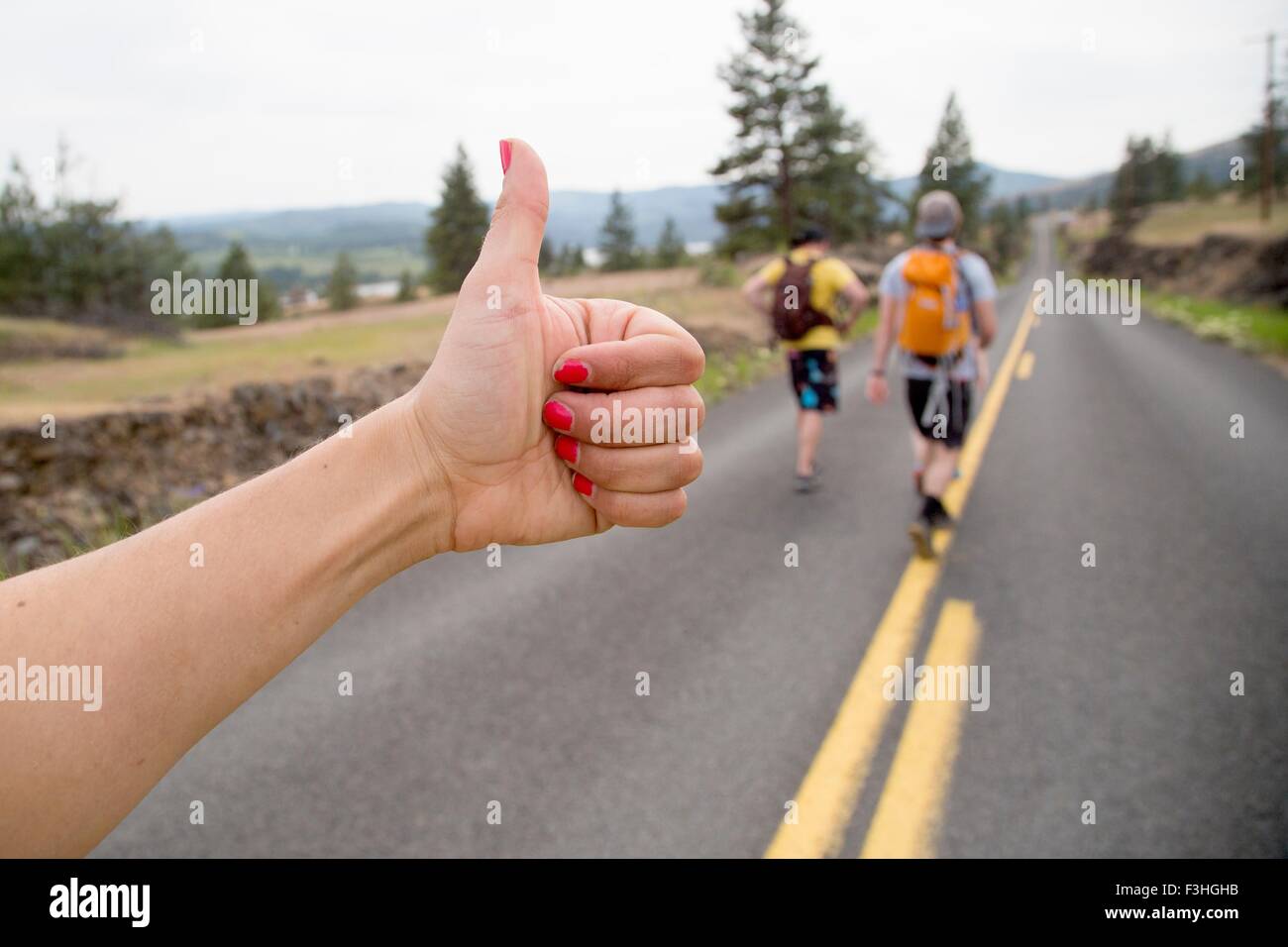 Two men hiking along road, while woman thumbs a lift, focus on hand ...
