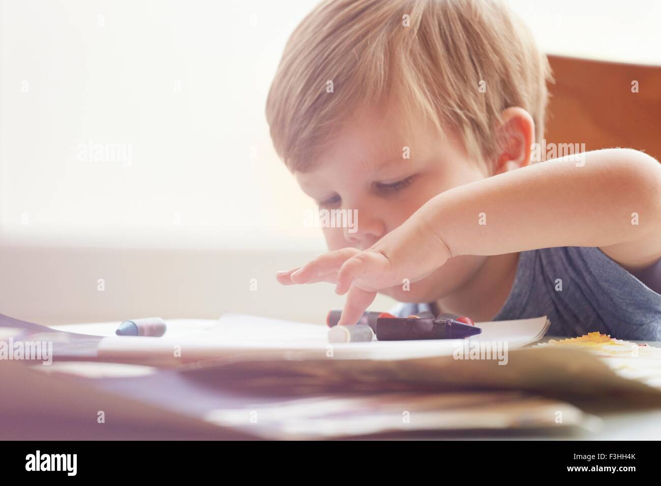 Boy sitting at table rolling crayons with finger, looking down Stock ...