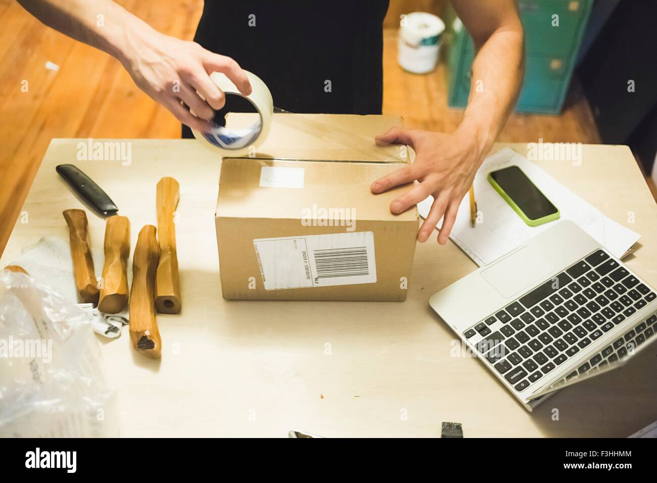High angle view of young mans hands using sticking tape to prepare ...