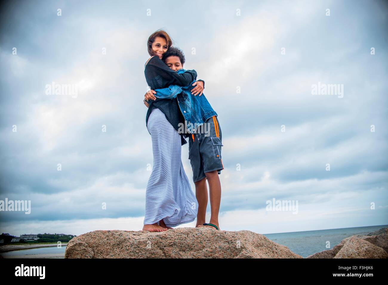 Portrait of mature woman and son hugging on coastal rocks Stock Photo ...