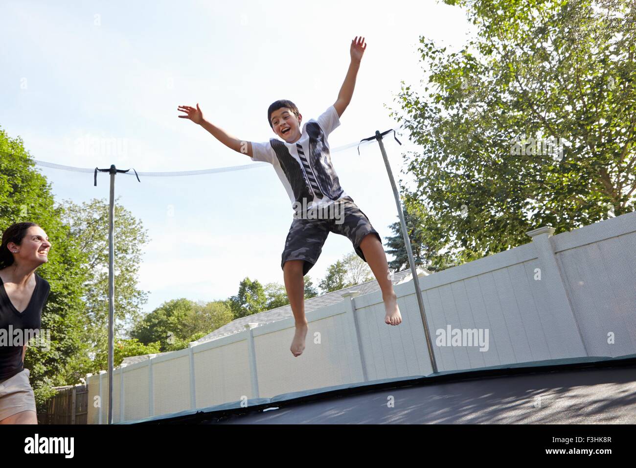Mother watches son jumping on trampoline in garden Stock Photo - Alamy