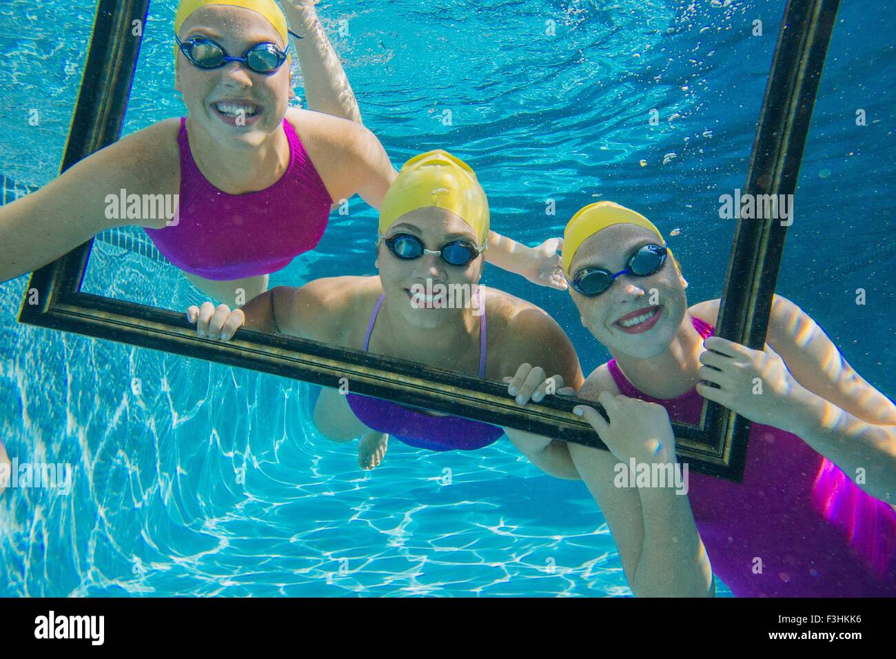 Three female swimmers, underwater, looking through frame Stock Photo ...