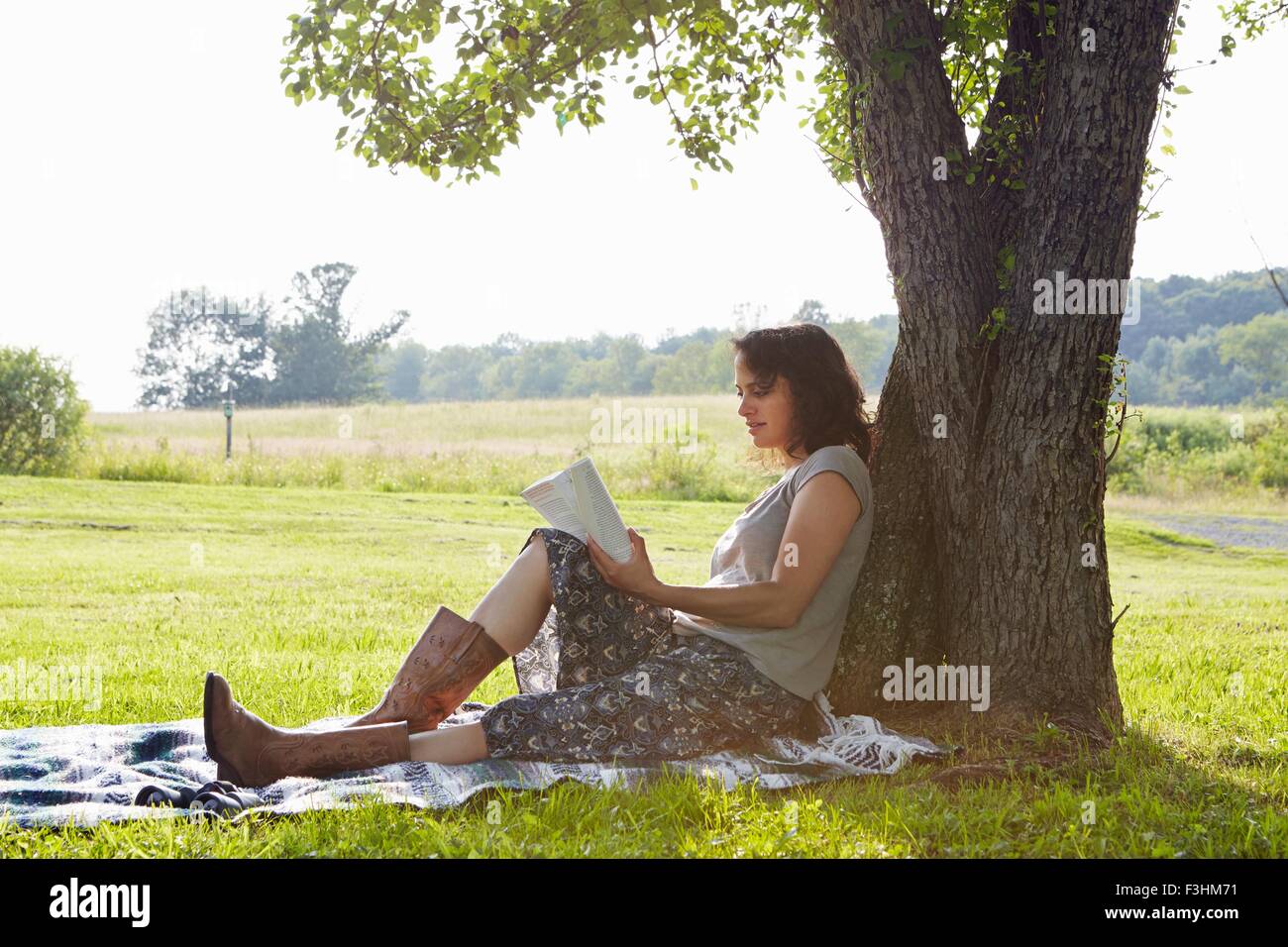 Woman reading book whilst leaning against tree Stock Photo - Alamy