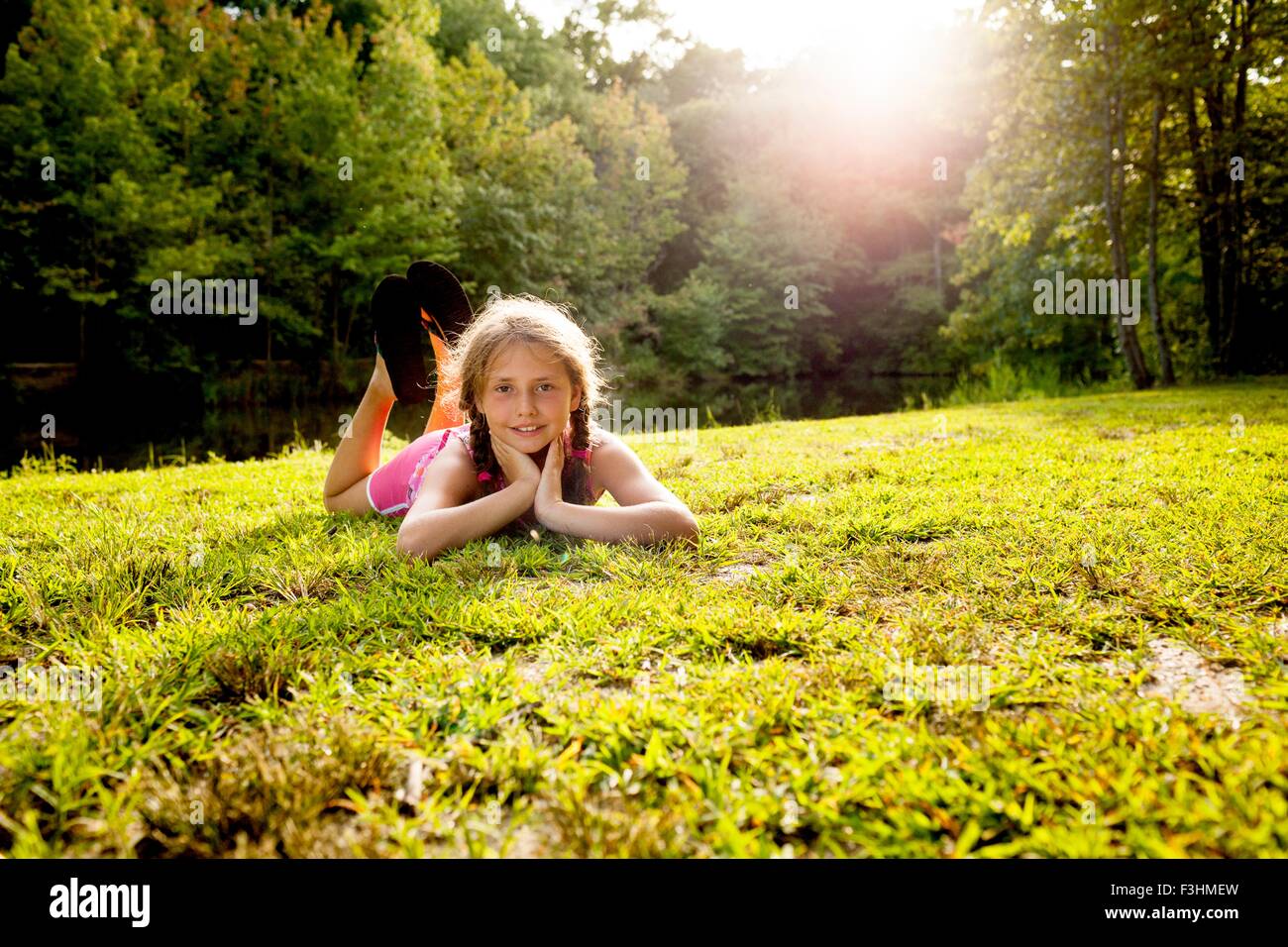 Surface level view of girl lying on front on grass looking at camera ...