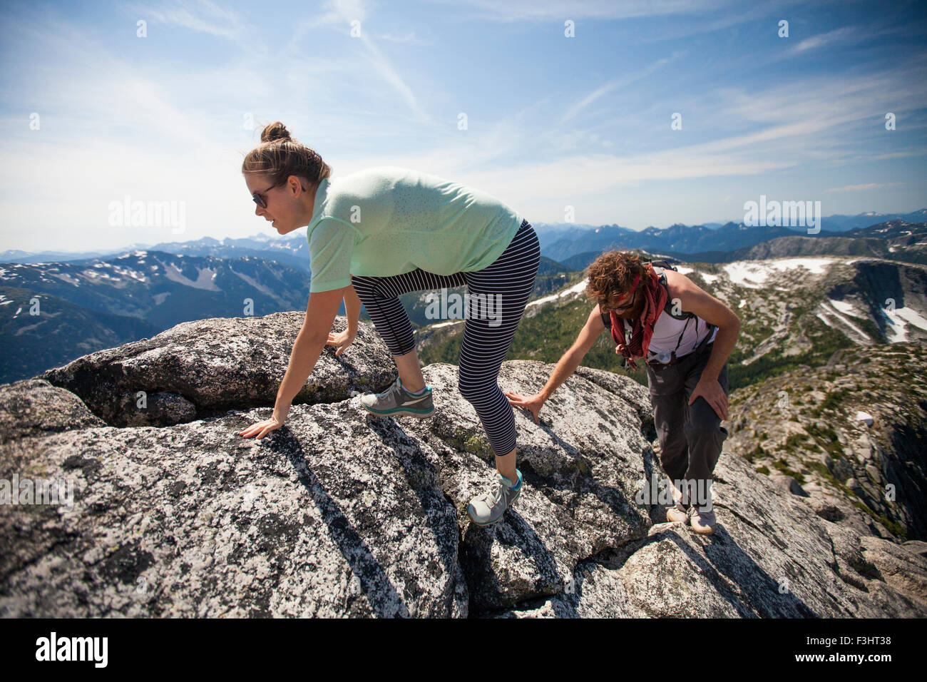 A man and woman scramble over granite rock on a mountain ridge Stock ...