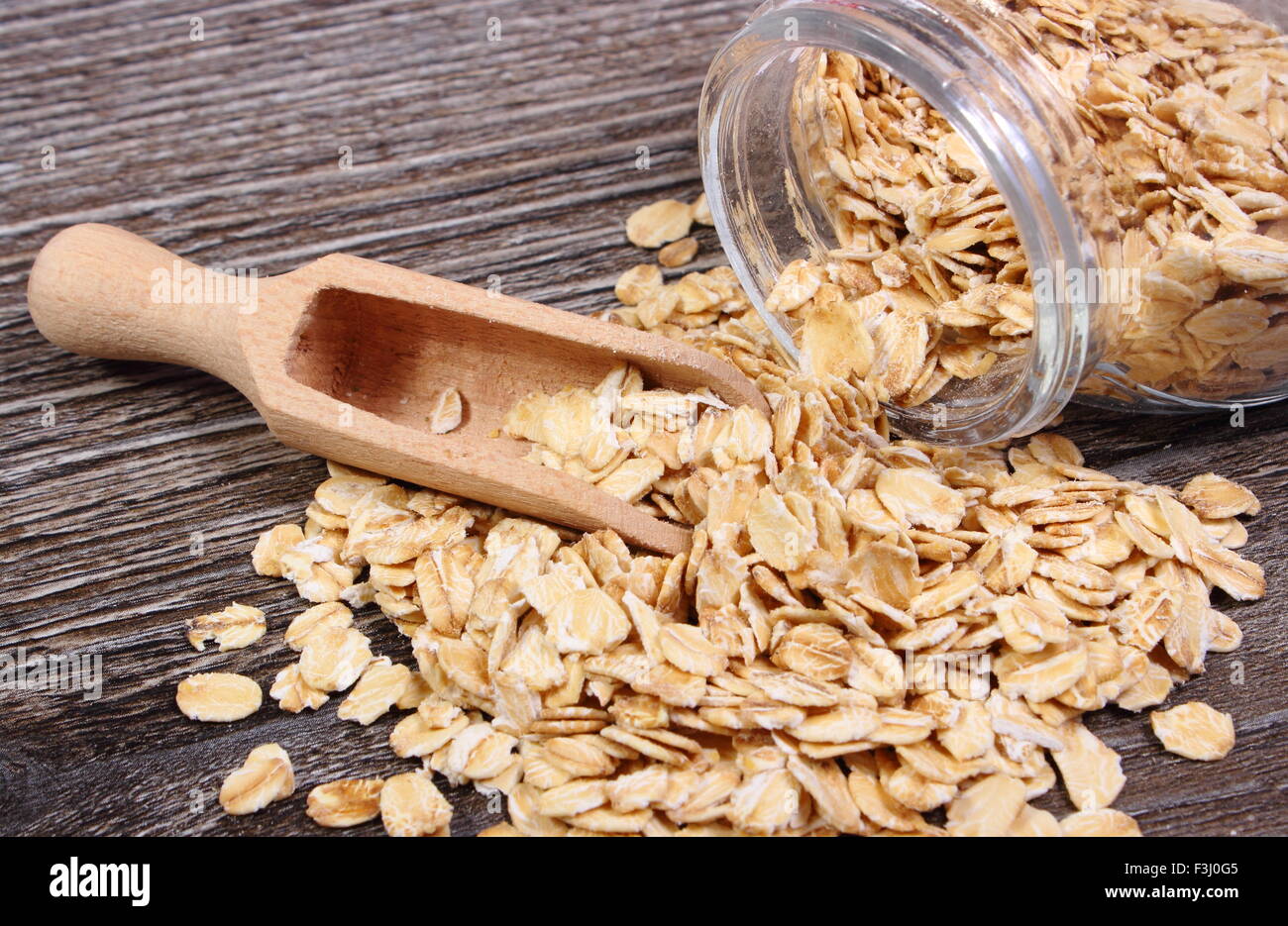 Heap of organic oatmeal, oat flakes spilling out of glass jar on wooden ...