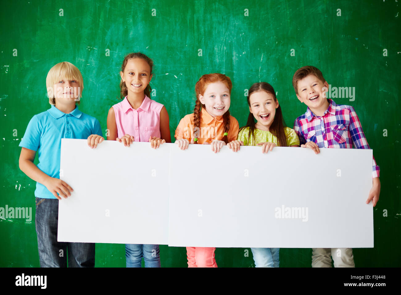 Friendly schoolkids with blank paper standing against blackboard Stock ...