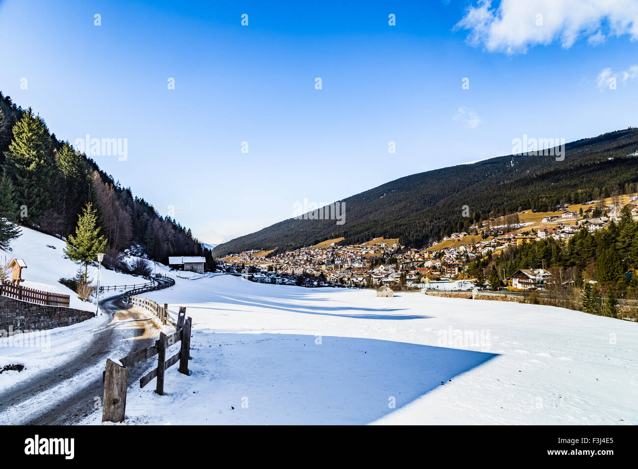 Snowy alpine village in Italy illuminated by sun with mountains in the ...