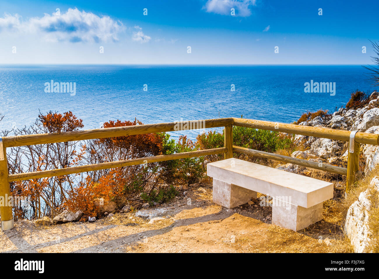 stone bench and wooden parapet on steep cliffs above the sea along the coast of Puglia in Italy ...
