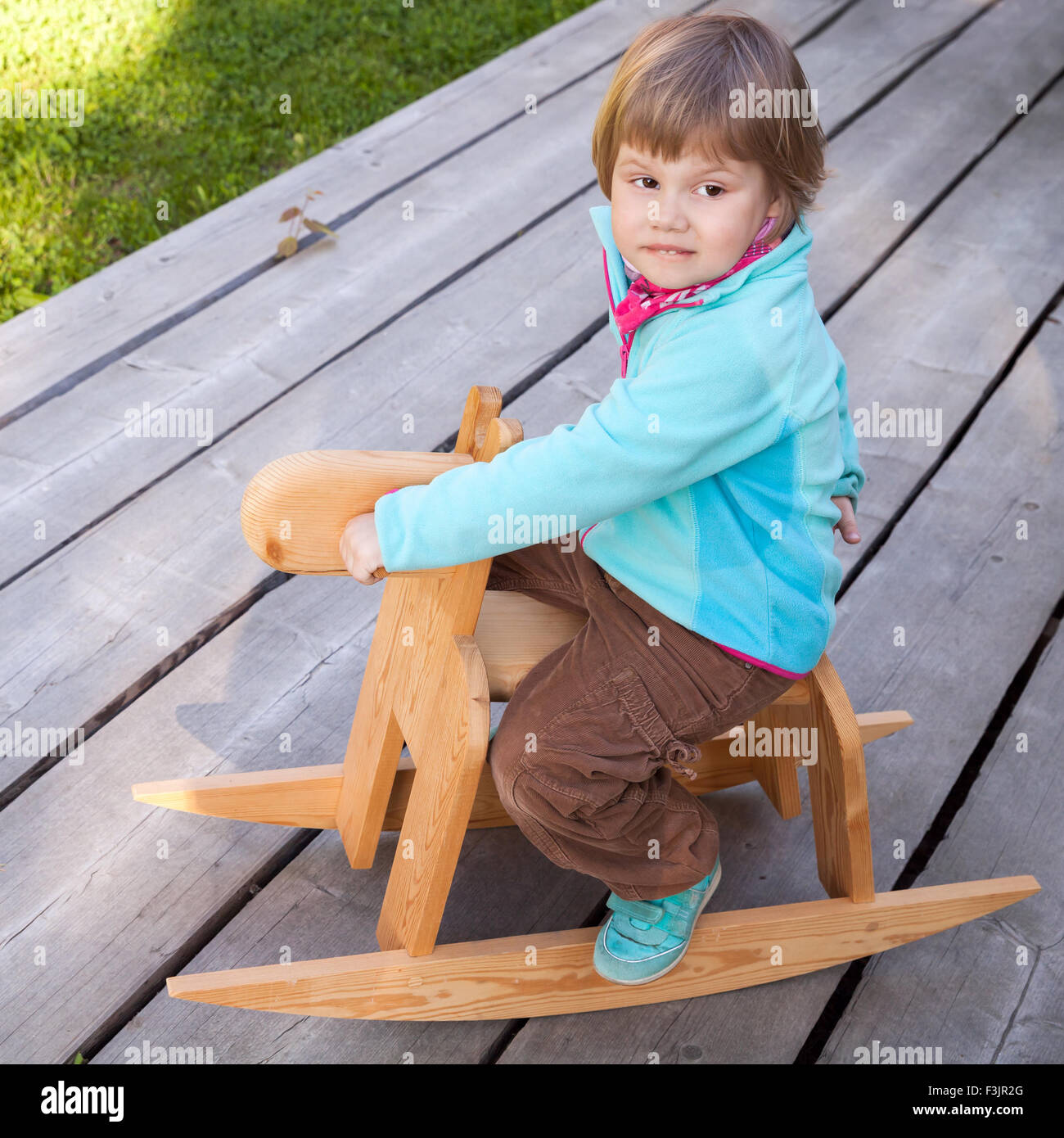 Outdoor portrait of cute Caucasian blond baby girl riding small wooden ...