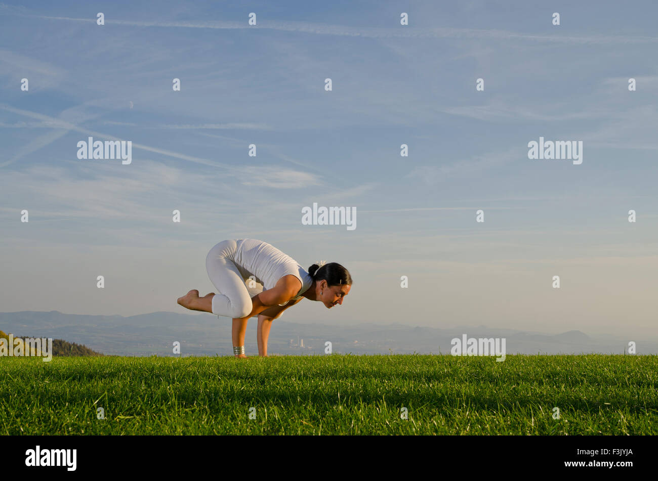 Young woman practising Hatha-Yoga outdoor, showing the pose kakasana ...