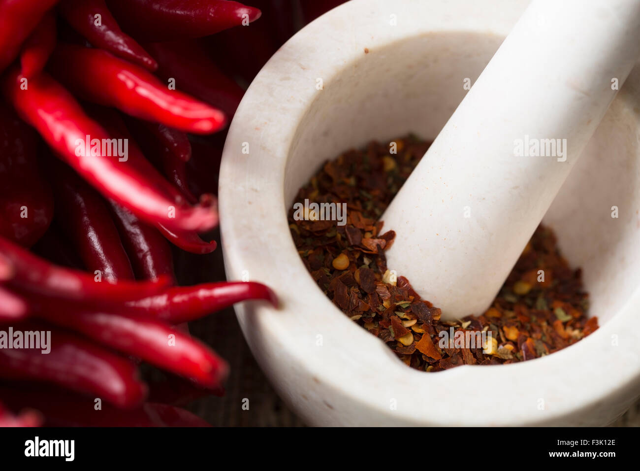 Crushed hot red pepper flakes in a mortar and pestle and fresh peppers ...
