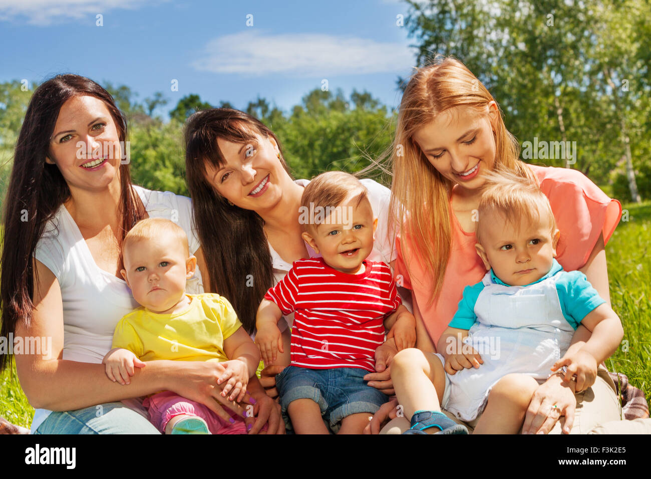 Three women with their babies sit on green grass Stock Photo - Alamy