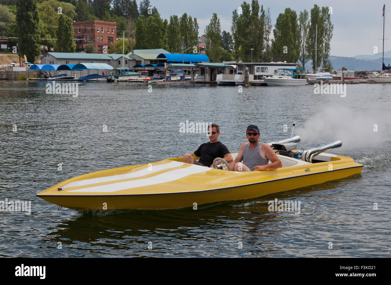 Two men in a yellow speedboat going slow through a marina with boats ...