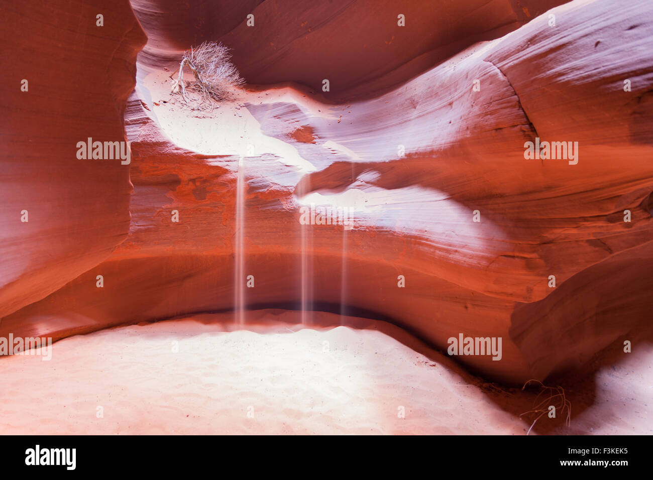 Sand cascading from a rock ledge below a tumbleweed lit from above in ...
