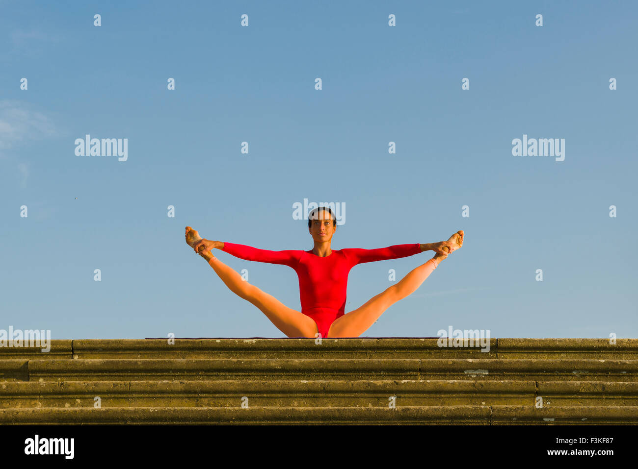 Young woman, wearing a red-orange body suit, is practising Hatha-Yoga ...
