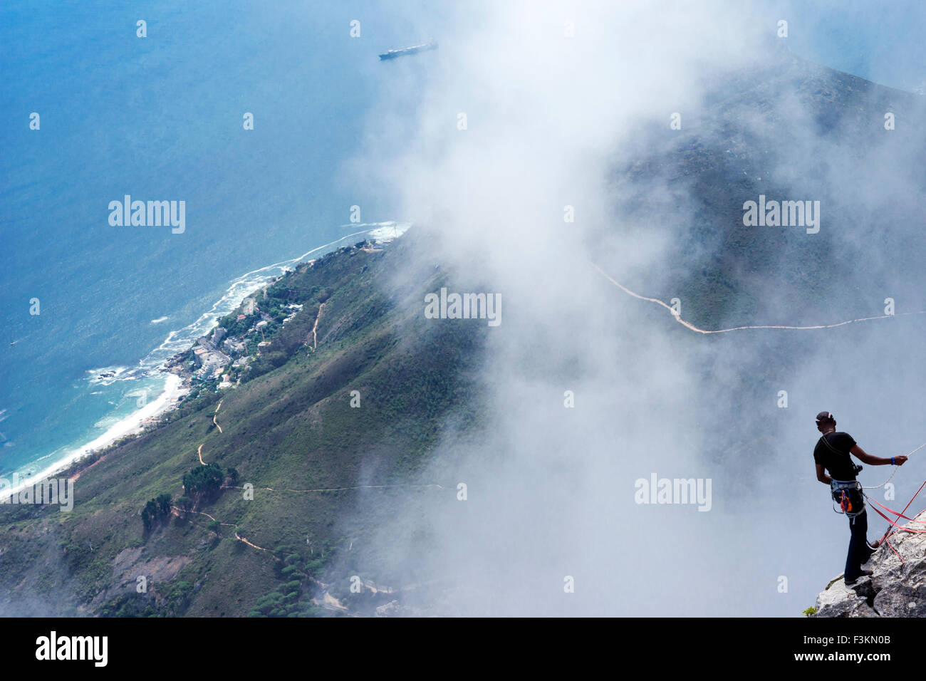 Male guide looks over the cliff where someone is rappelling, or ...
