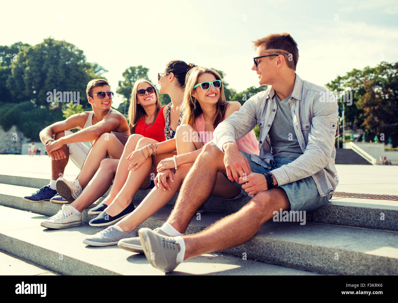 group of smiling friends sitting on city street Stock Photo - Alamy