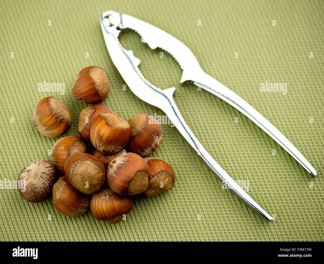 Un-opened hazelnuts with nut cracker on green background Stock Photo ...