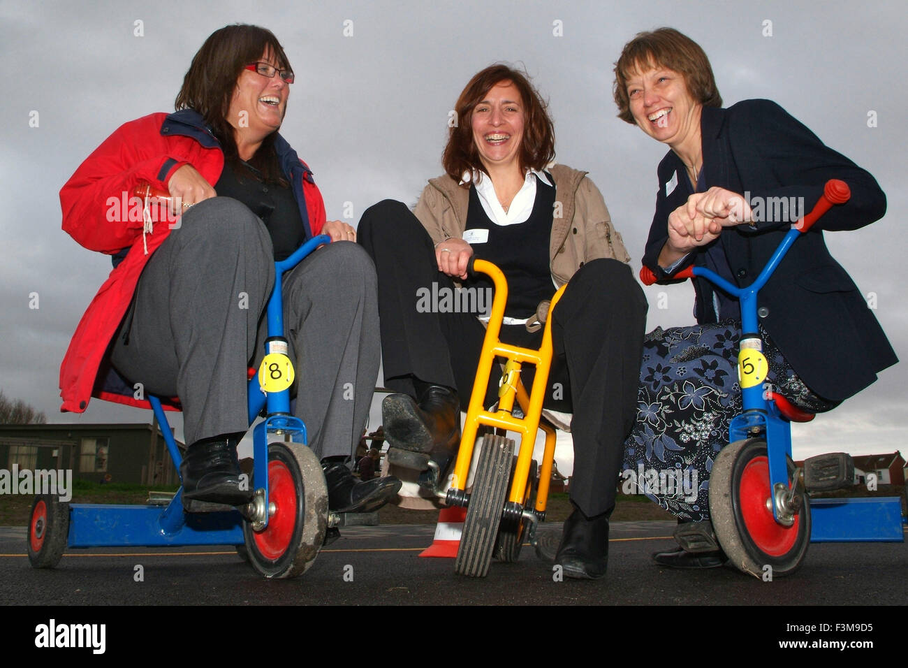Three (3) women teachers having fun riding childrens small cycles at ...