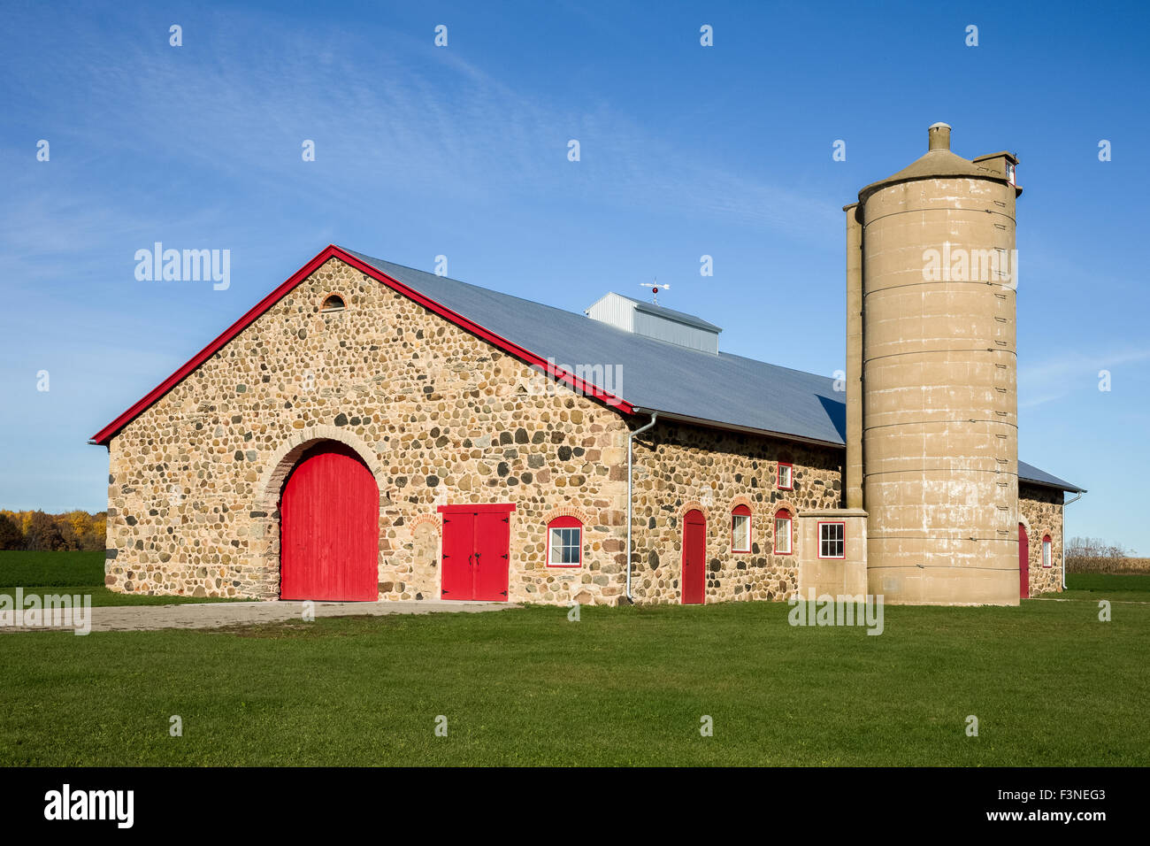 Retro field stone barn with bright red doors set against a blue sky ...