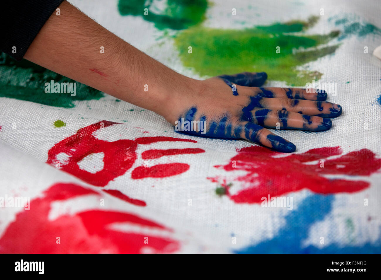 Applying hand print painting on canvas among other coloured hand ...