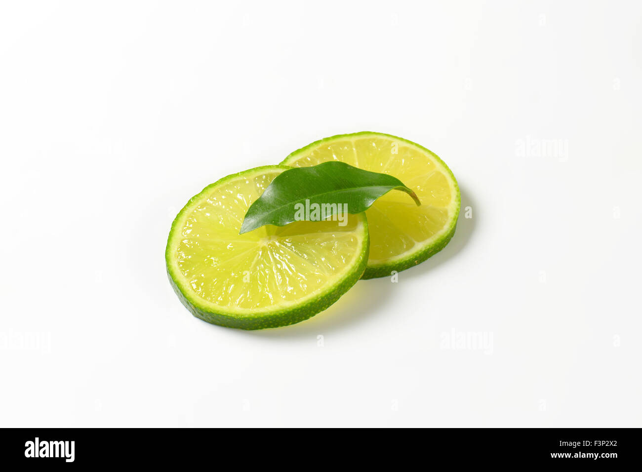 two lime slices with leaf on white background Stock Photo - Alamy