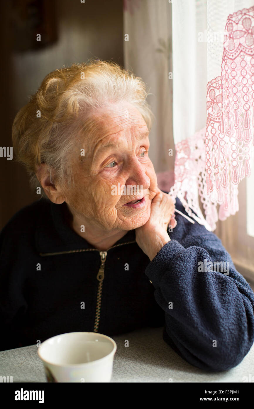 An elderly lady sitting near the window in the kitchen Stock Photo - Alamy
