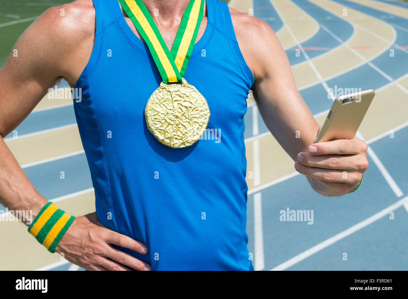 Gold medal athlete standing at running track using his mobile phone ...