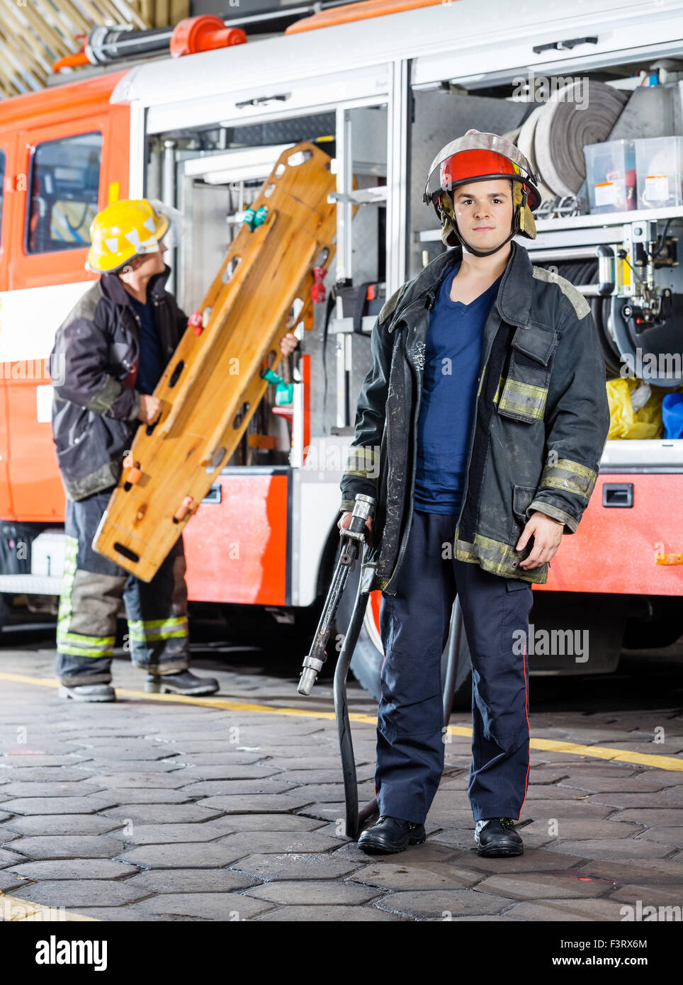 Firefighter Holding Hose While Colleague Carrying Stretcher Stock Photo ...