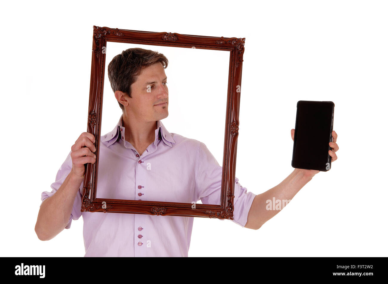 A young man holding up a picture frame, looking trough on his tablet ...