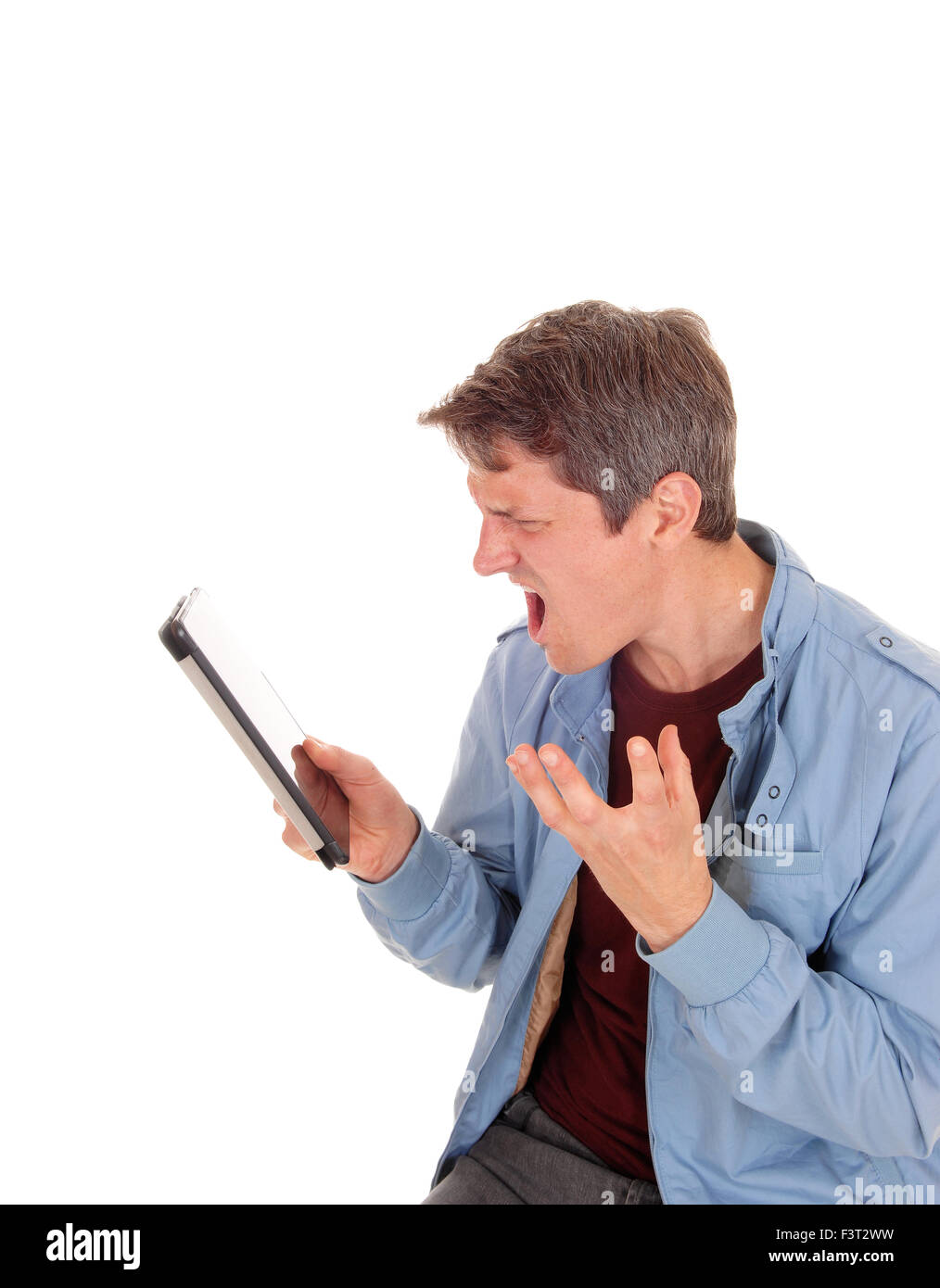 A young man in a blue jacket holding his tablet and shouting at it ...