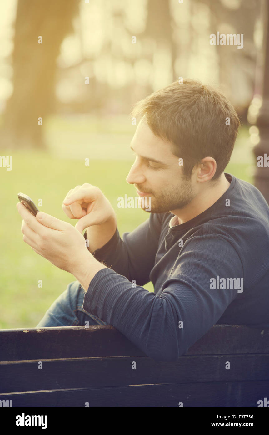 Young man sitting in the park and texting a message Stock Photo - Alamy