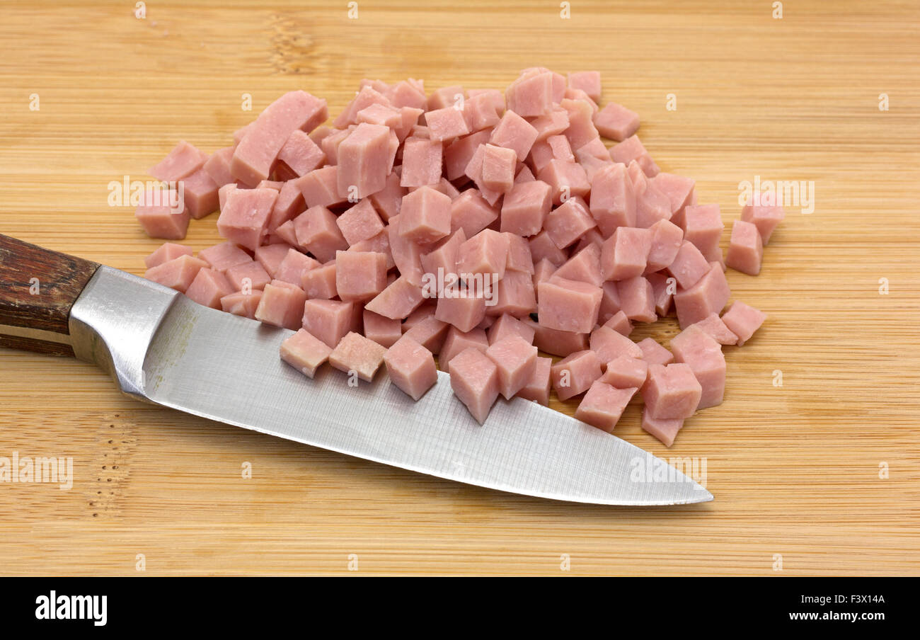 A portion of diced ham on a wood cutting board with a kitchen knife ...