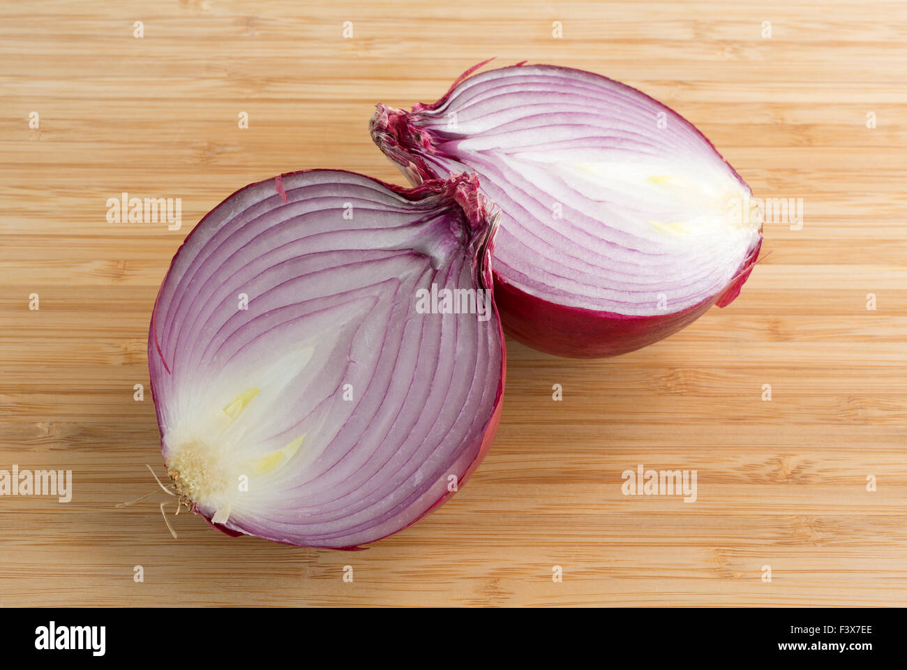 A large red onion that has been sliced in half on a wood cutting board ...