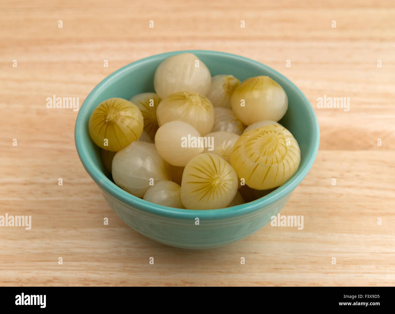 A small green bowl filled with cooked small onions on a wood table top ...