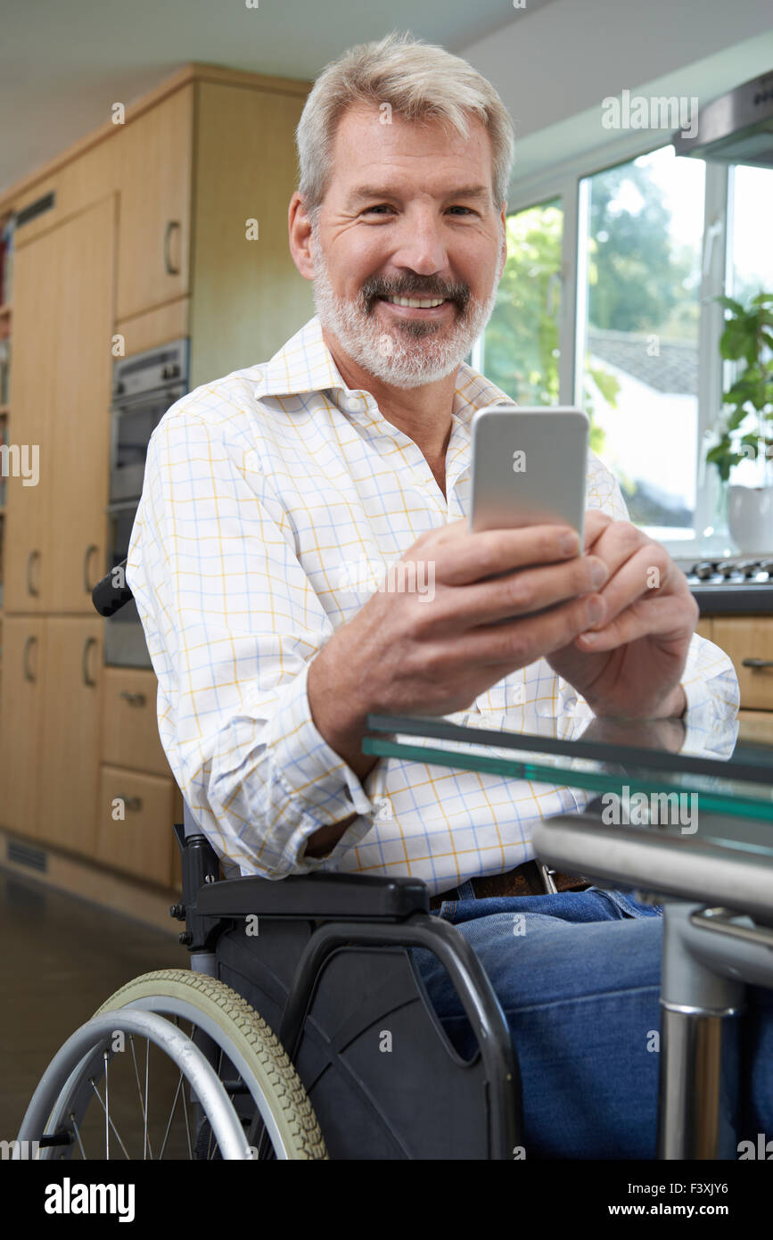 Disabled Man In Wheelchair Texting On Mobile Phone At Home Stock Photo ...