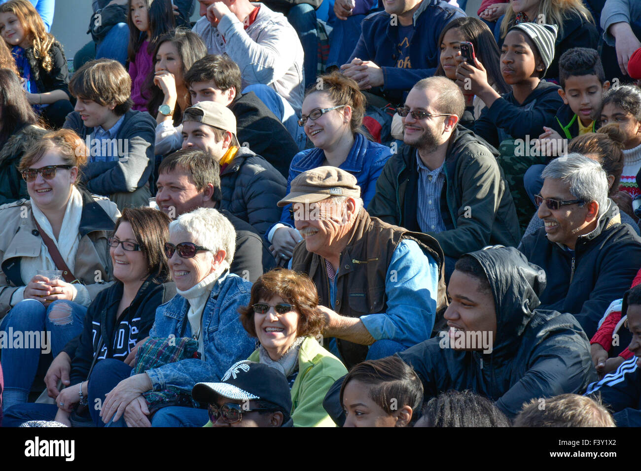 Multitude of diverse people in the USA sitting on bleachers reacting ...