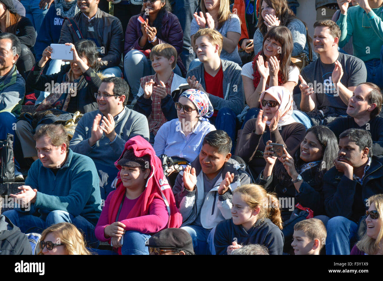 Multitude of diverse people in the USA sitting on bleachers reacting ...