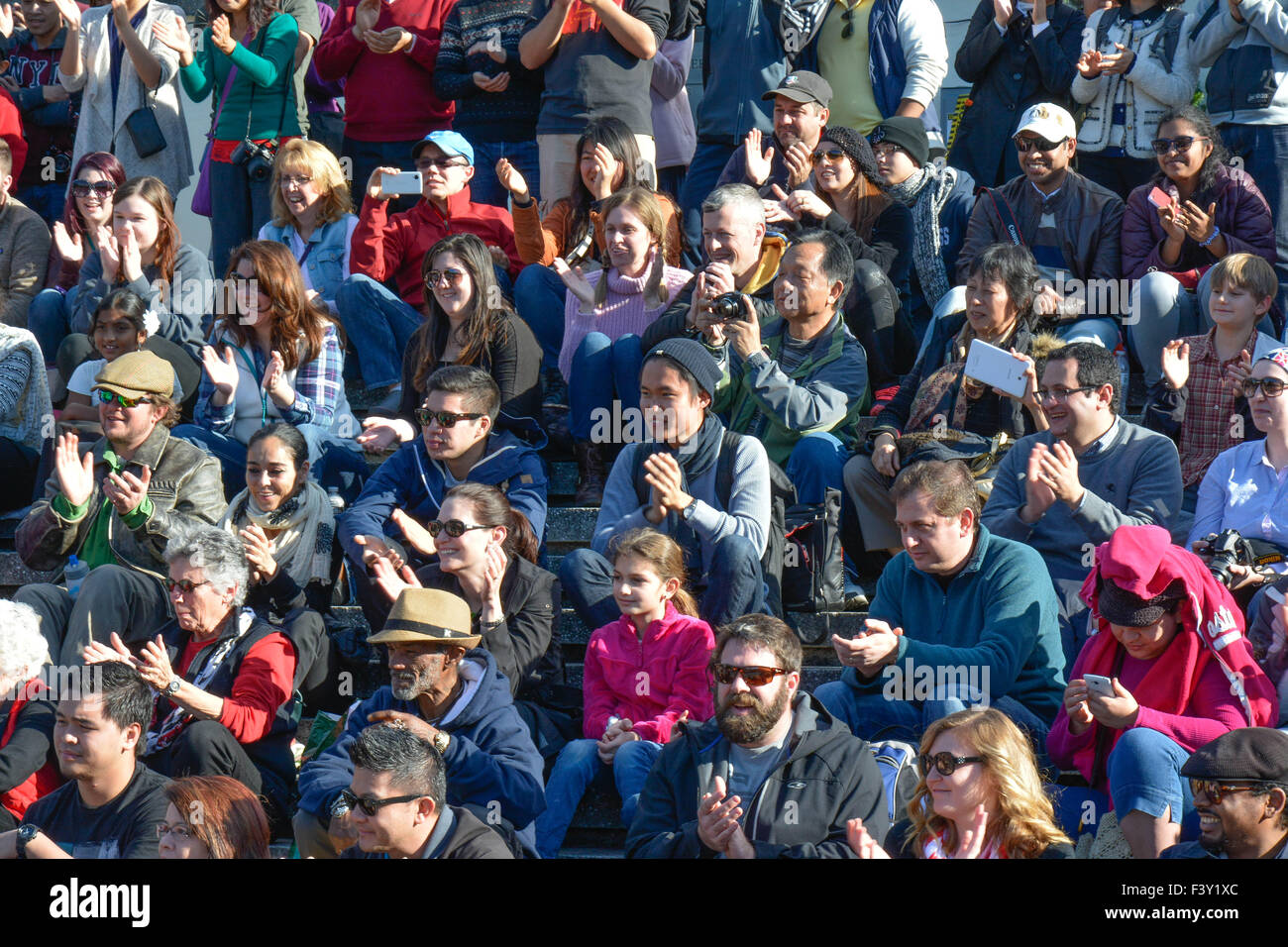 Multitude of diverse people in the USA sitting on bleachers reacting ...