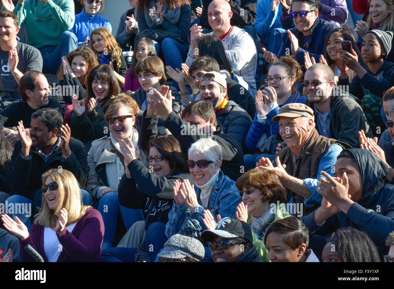 Multitude of diverse people in the USA sitting on bleachers reacting ...