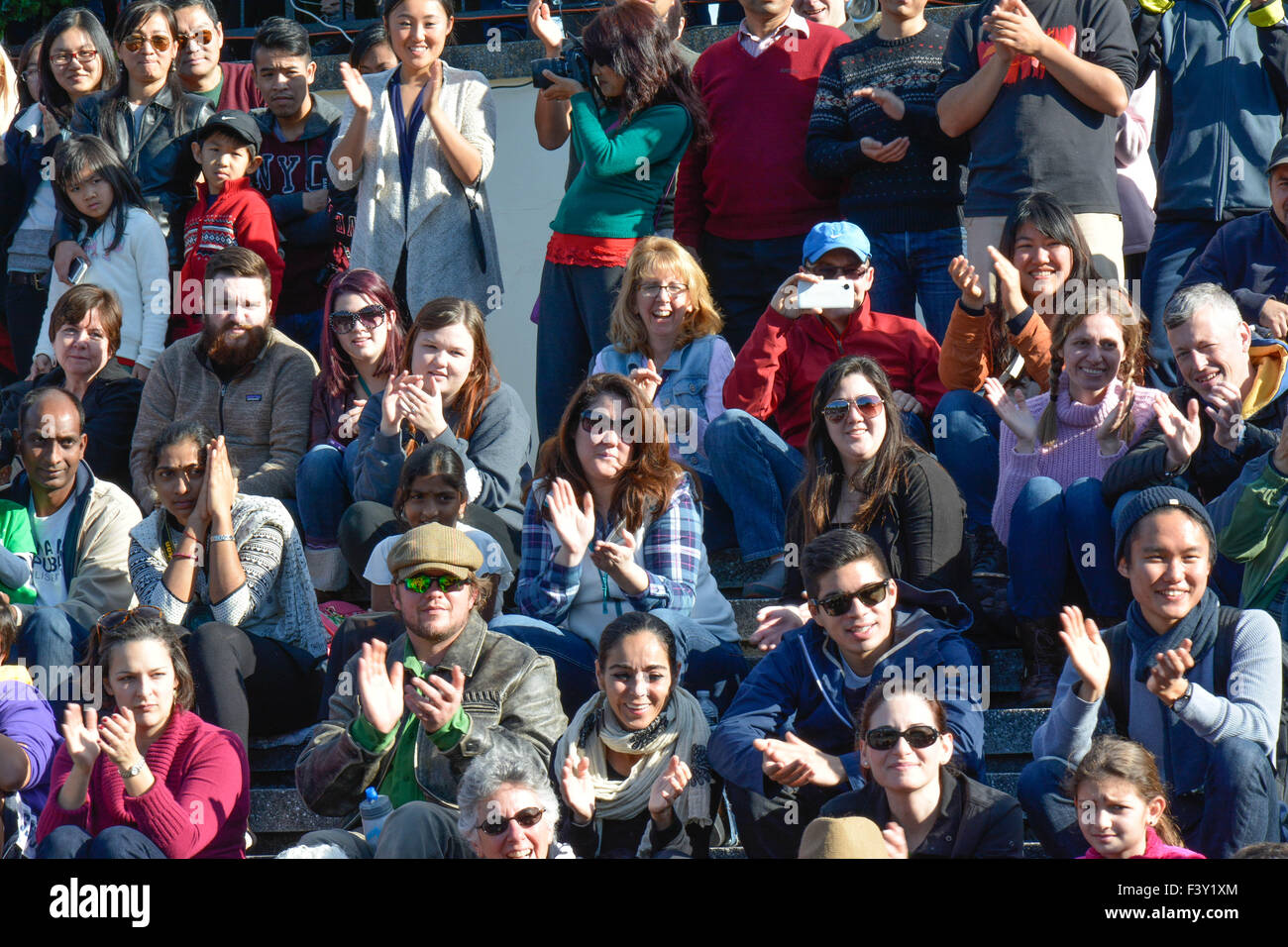 Multitude of diverse people in the USA sitting on bleachers reacting ...