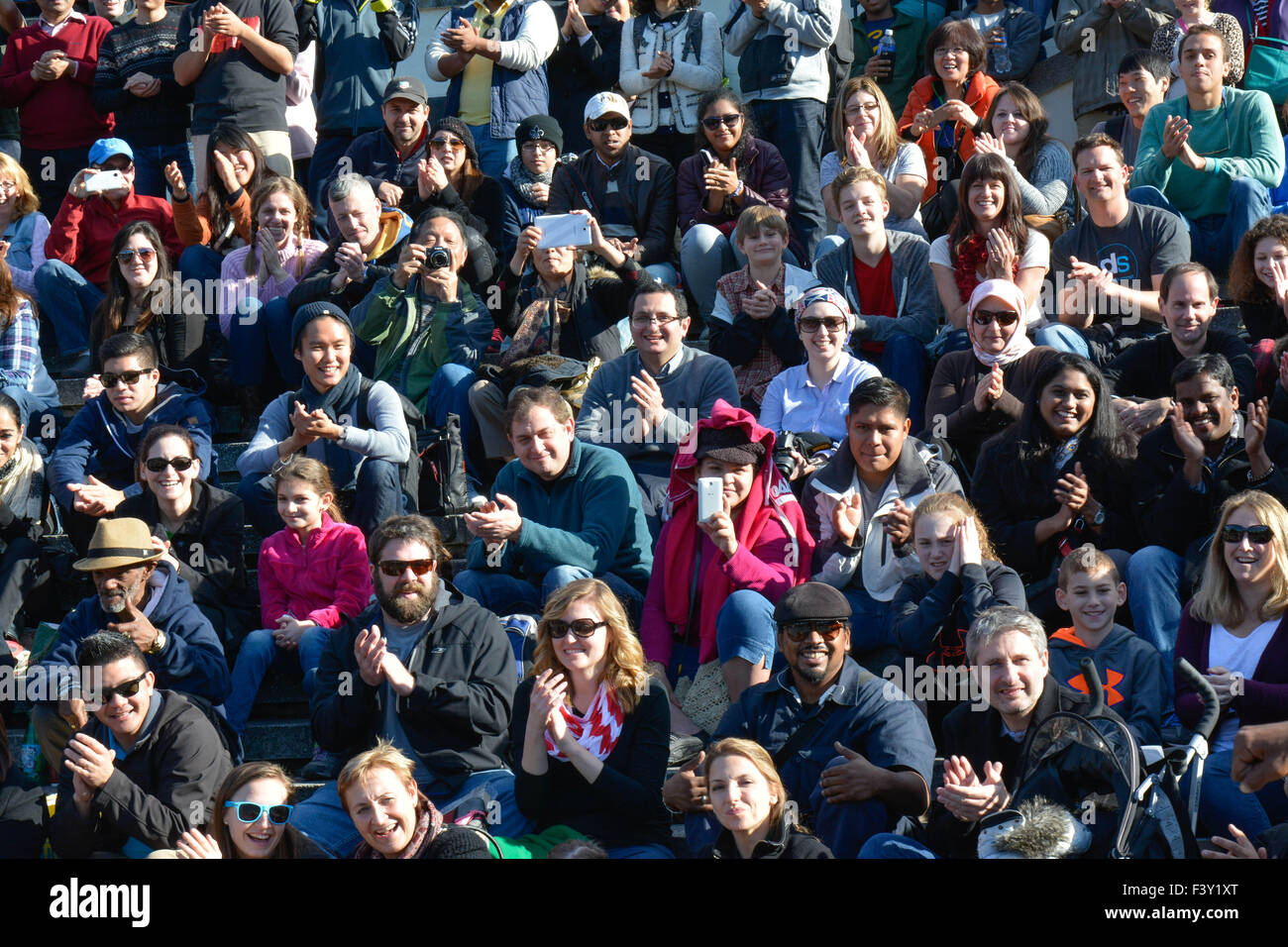Multitude of diverse people in the USA sitting on bleachers reacting ...