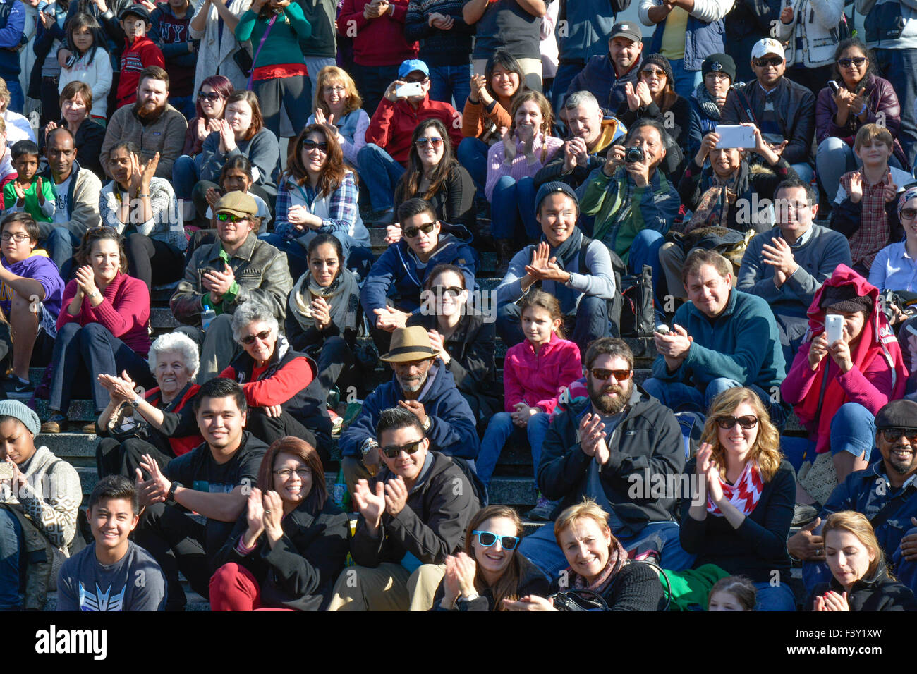 Multitude of diverse people in the USA sitting on bleachers reacting ...