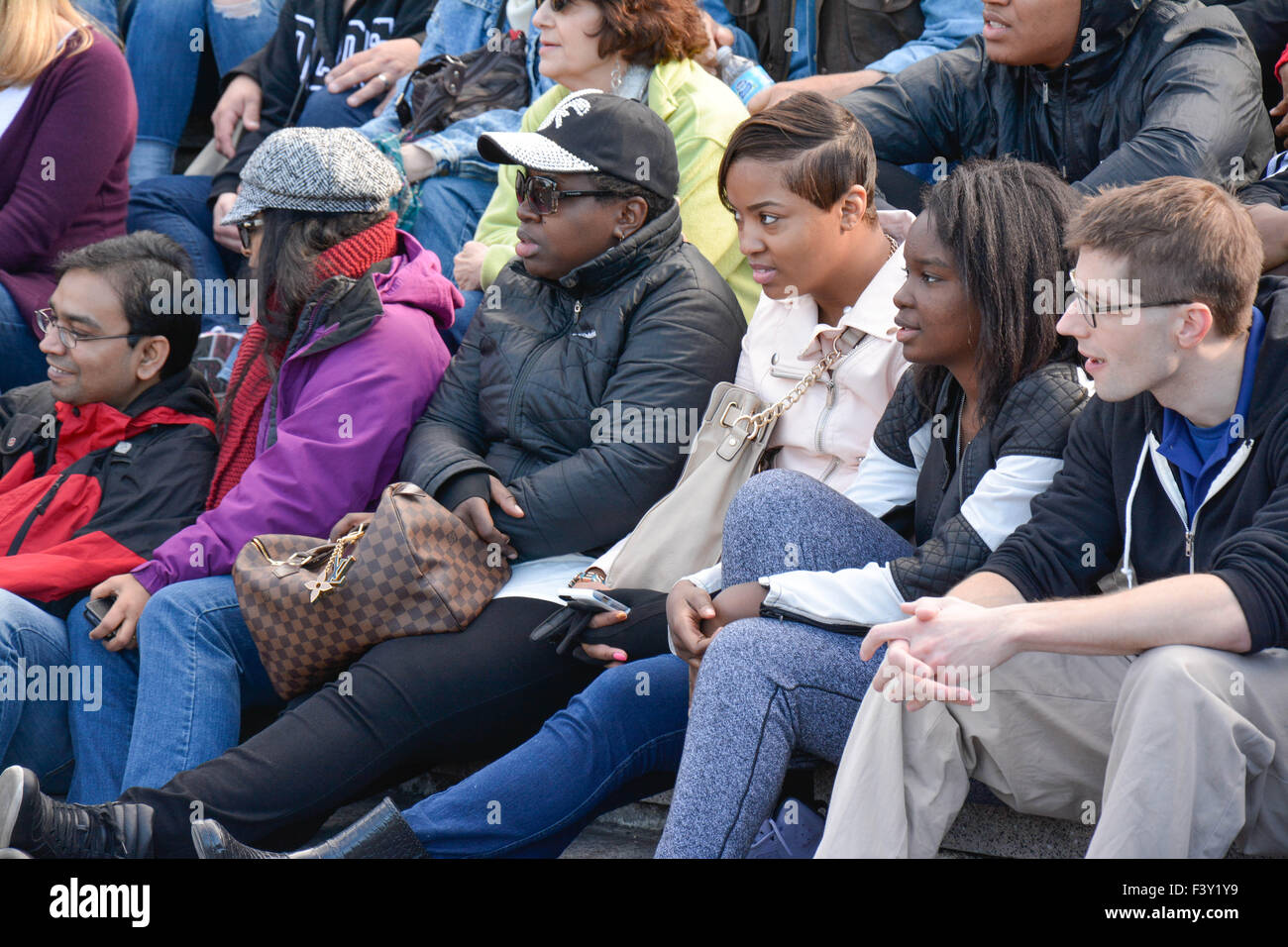 Multitude of diverse people in the USA sitting on bleachers reacting ...