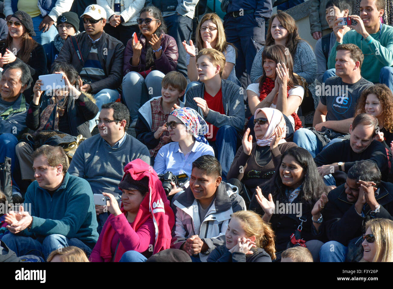 Multitude of diverse people in the USA sitting on bleachers reacting ...