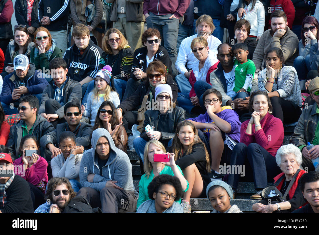 Multitude of diverse people in the USA sitting on bleachers reacting ...